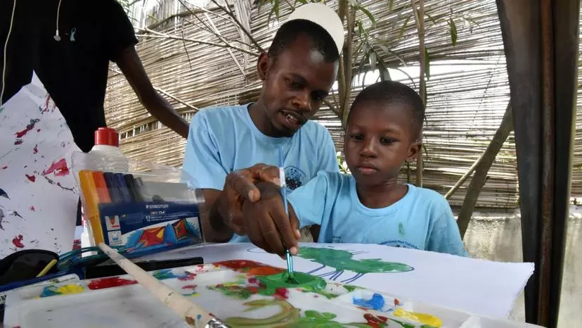 Un home axuda a pintar a un neno con autismo en Abidjan, Costa de Marfil. Os pais de nenos con autismo son máis propensos a lembrar que o seu fillo foi inmunizado antes de mostrar sinais de autismo e establecer unha conexión, aínda que sexa incorrecta: un exemplo de sesgo de lembranza SIA KAMBOU/AFP/Getty Images