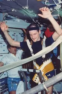 Astronot G. David Low nggunakake treadmill ing pesawat angkasa Columbia minangka fellow crewmembers Daniel C. Brandenstein lan James D. Wetherbee katon ing.